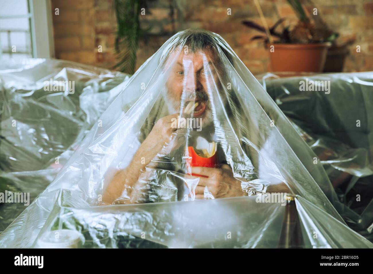Senior man covered with plastic, eating fast food - environmental ...