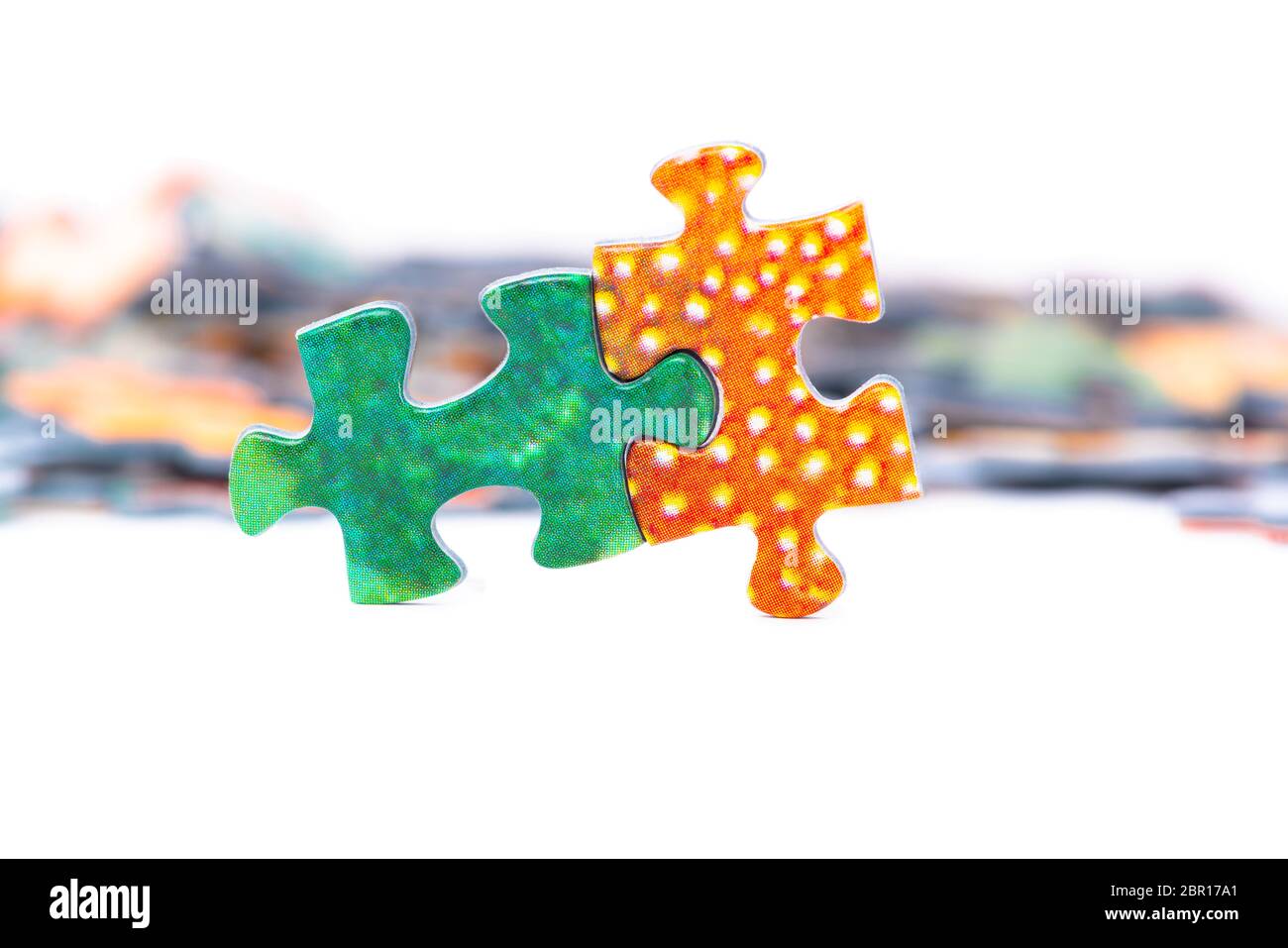 Two bright puzzle pieces connected in front of separated pieces. White ...