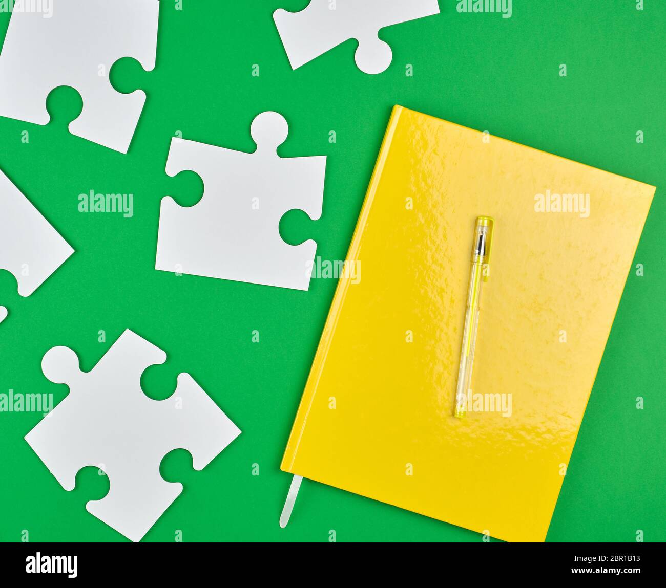 closed yellow notebook and pen, next to it are large empty white paper ...