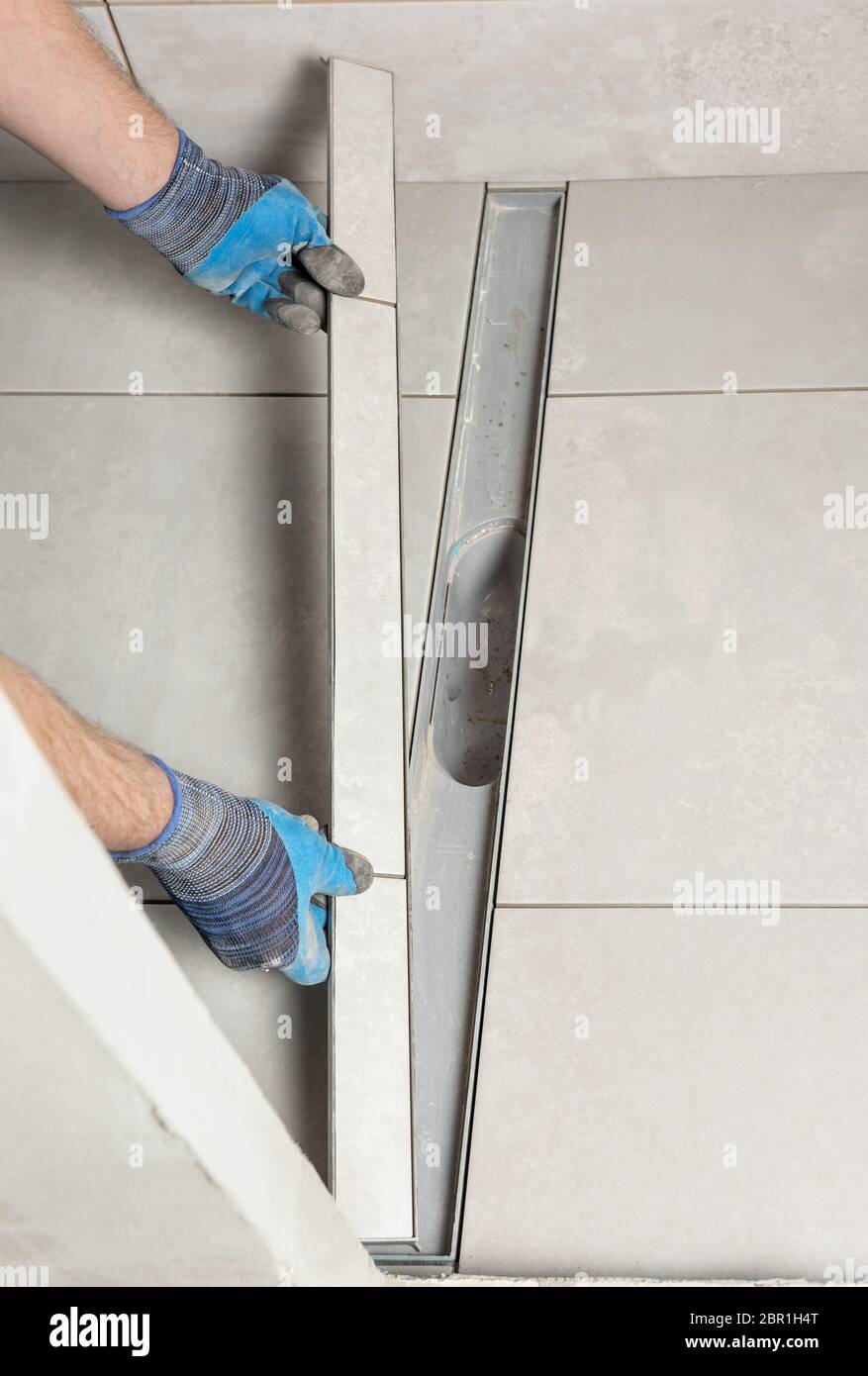 A worker is installing a drain lid decorated with ceramic tiles in the ...
