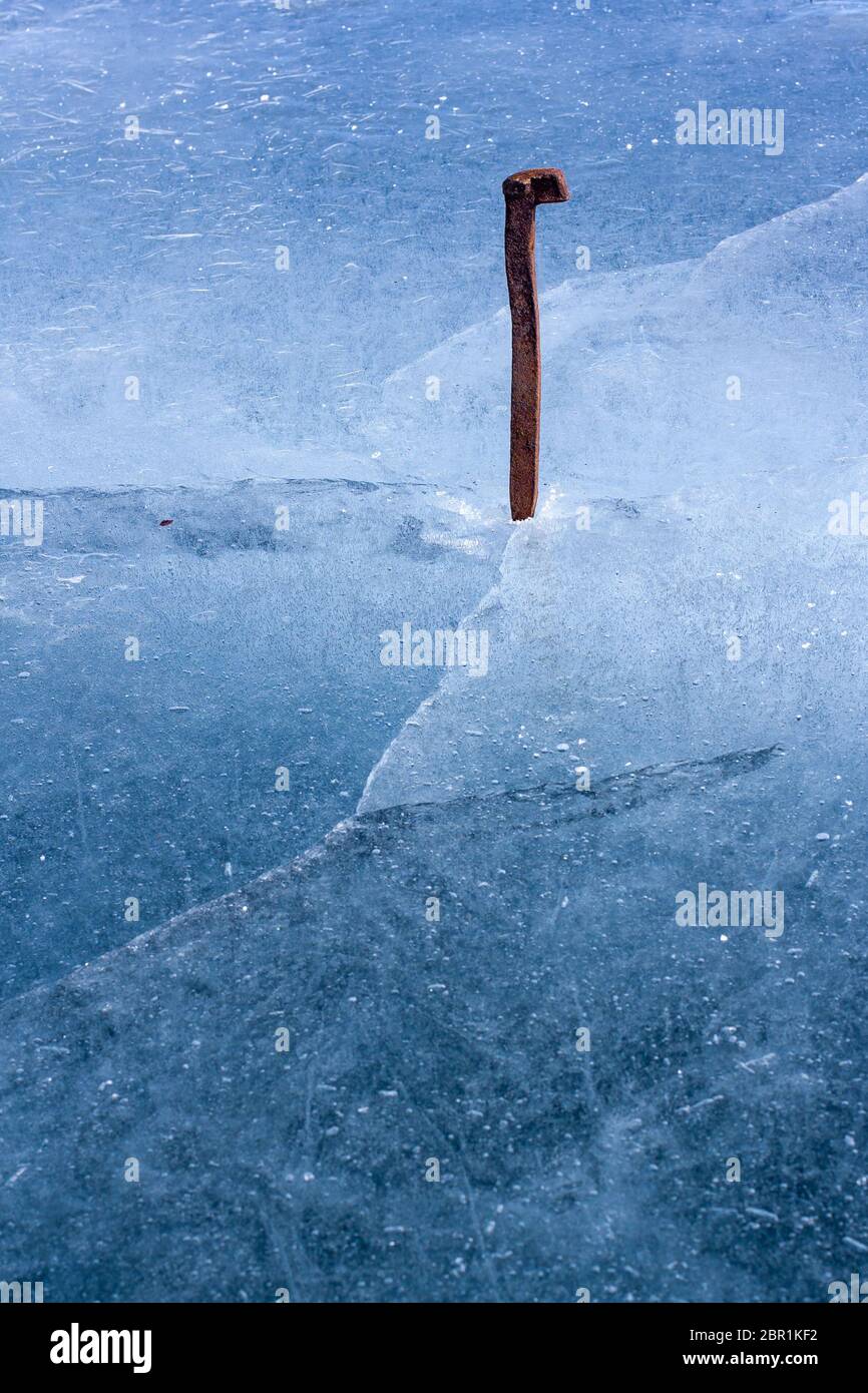 Rusty iron old railway crutch driven into ice. Blue melting ice with ...