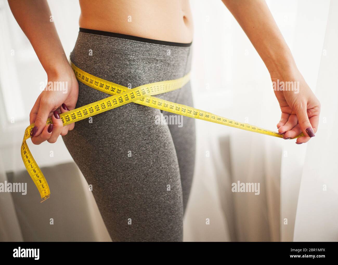 Hands measuring waist with a tape. Slim and healthy woman at her home ...