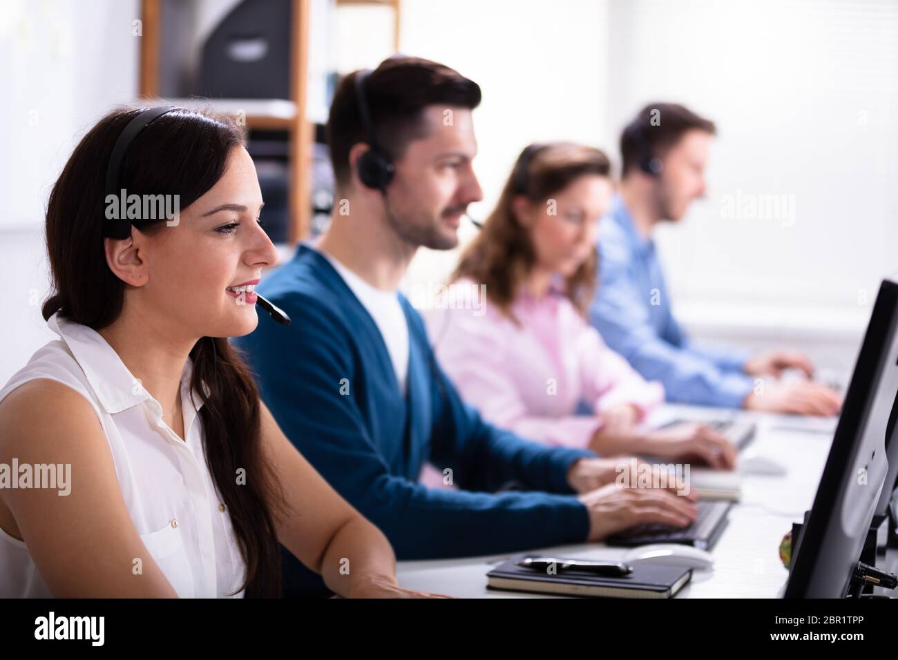 Happy Young Customer Service Executives Using Earphones Working In Call ...