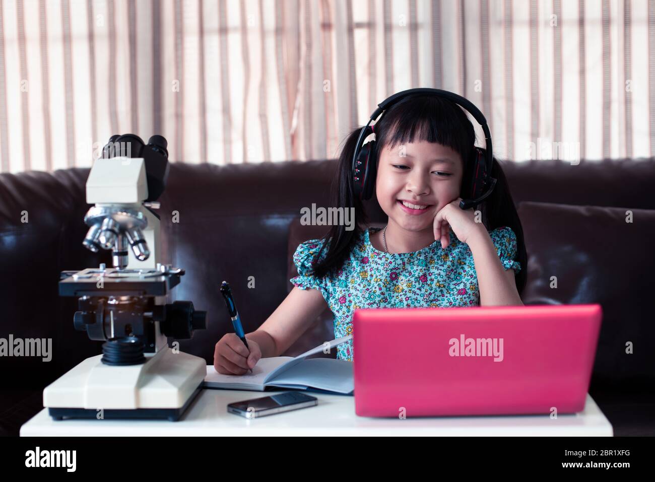 Asian little child girl wearing headphones learning online by using ...