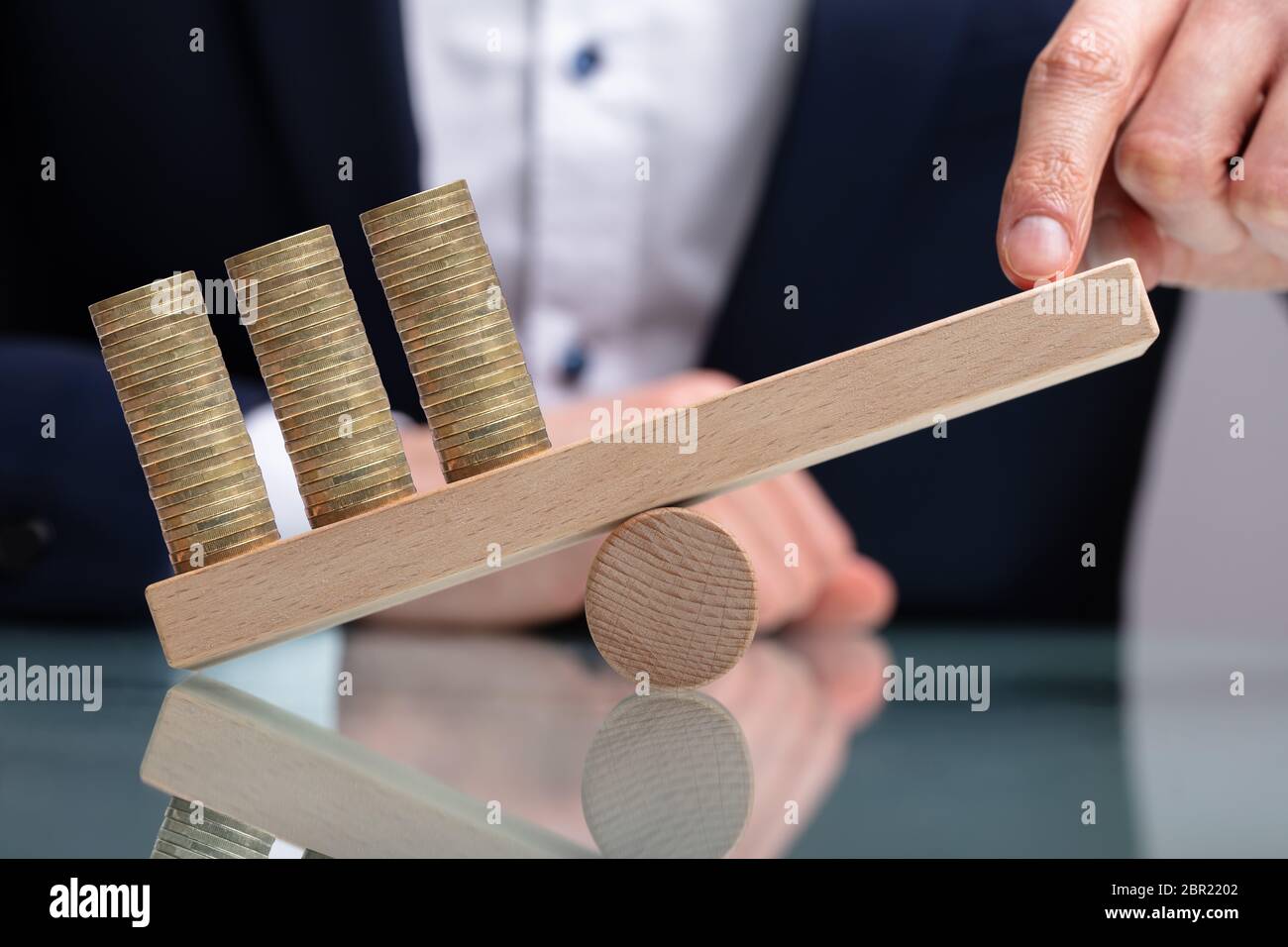 Businessman Balancing Stacked Coins With Finger On Wooden Seesaw Over ...