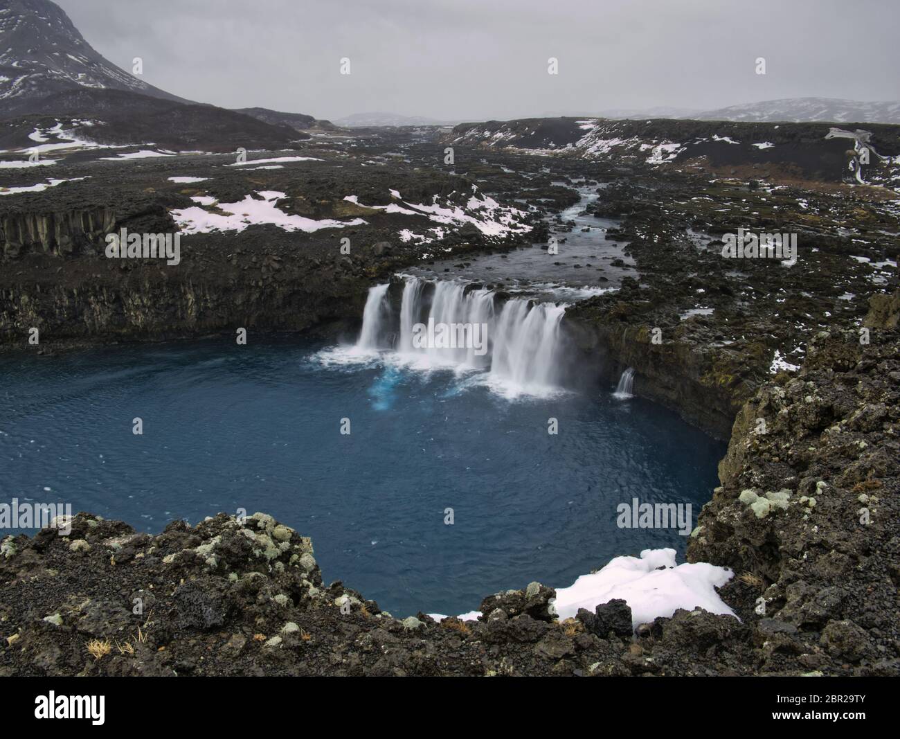 The blue water basin of the Thjofafoss waterfall in Iceland with snow ...