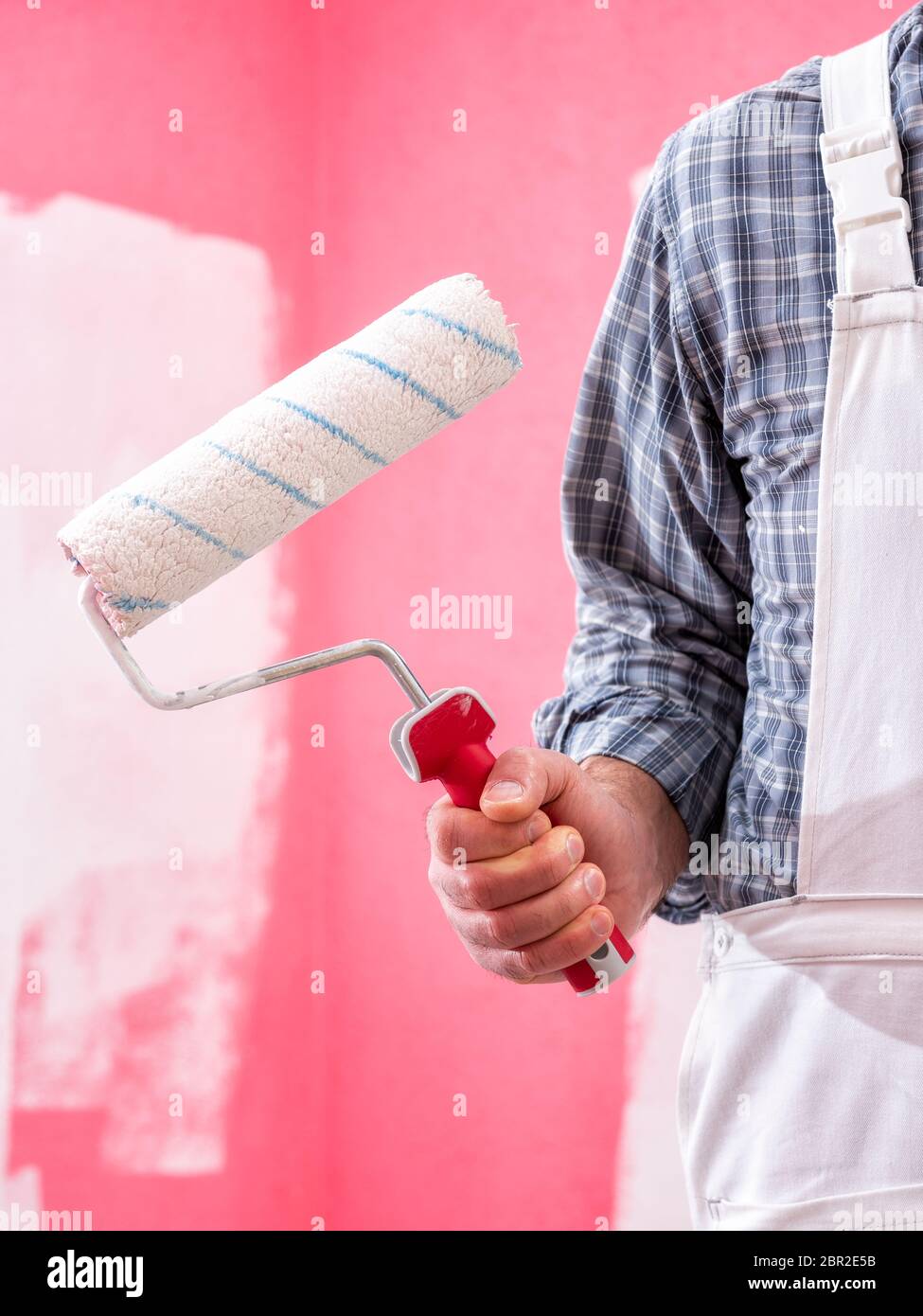 Caucasian house painter worker in white overalls, he holds the roller ...