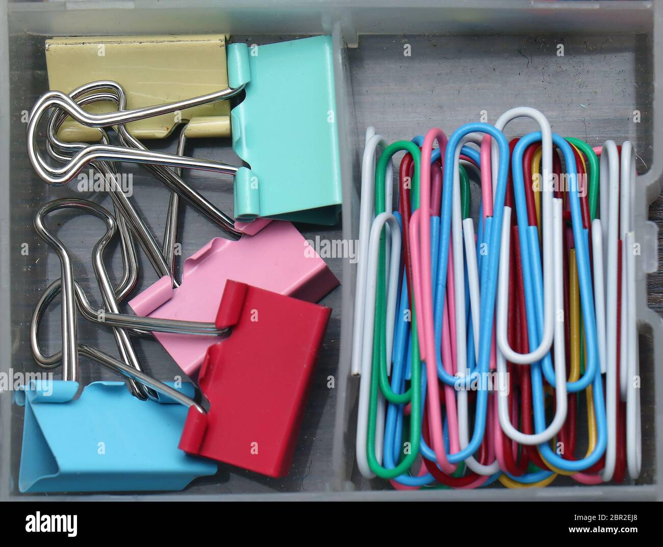 Colorful metal paperclips and binders piles stationery in plastic box ...