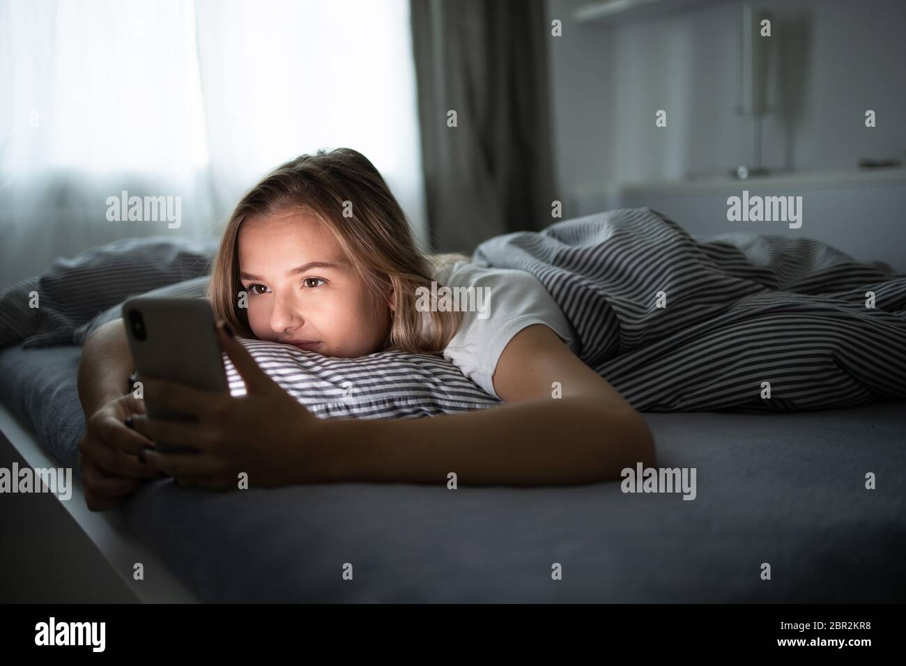 Pretty, young woman sleeping in her bed with her cell phone close to ...