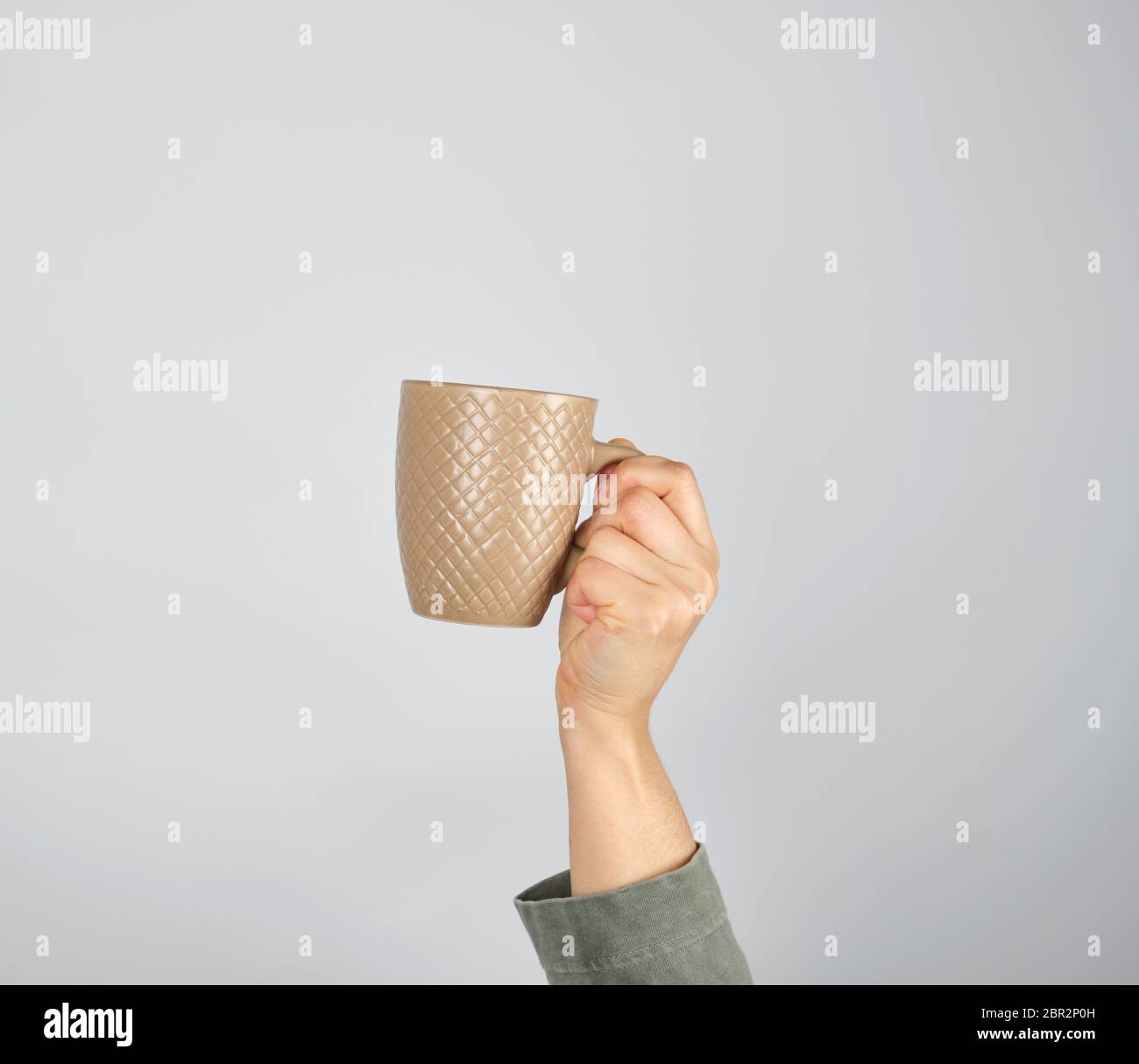 female hand holding a brown ceramic mug with a drink, gray background ...