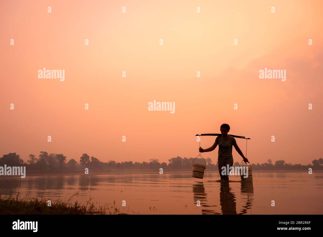 Young Cambodian woman collects water at twilight in Srah Srang, an ...
