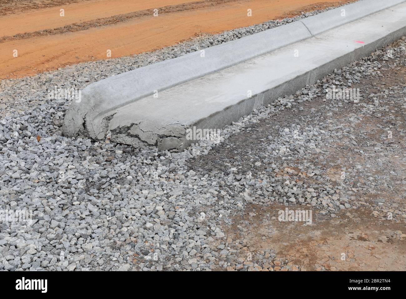 Cracked end of a section of extruded curb in gravel, road construction ...