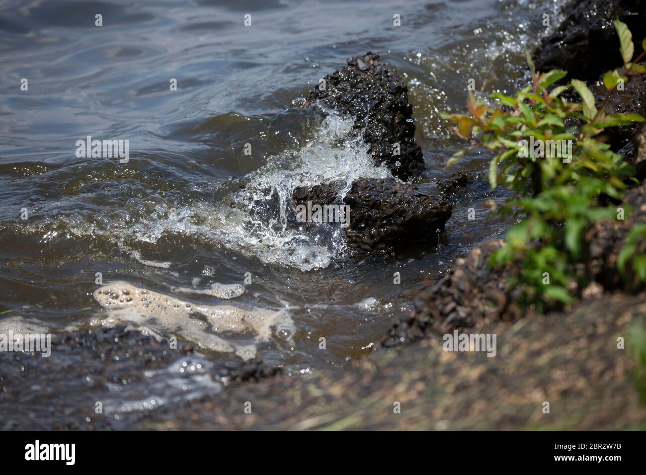 Light waves hitting rocks near a lake shore Stock Photo - Alamy
