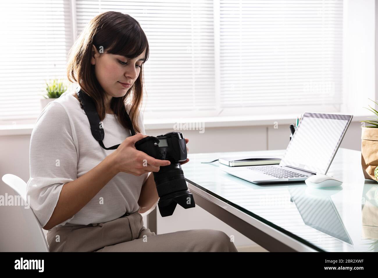 Female Editor Holding DSLR Camera With Laptop On Desk Stock Photo - Alamy