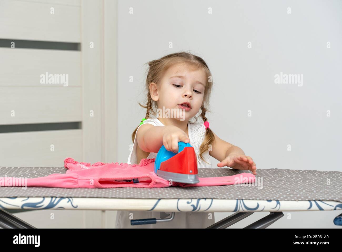 a pretty little girl of 4 years old plays a housewife, ironing children ...