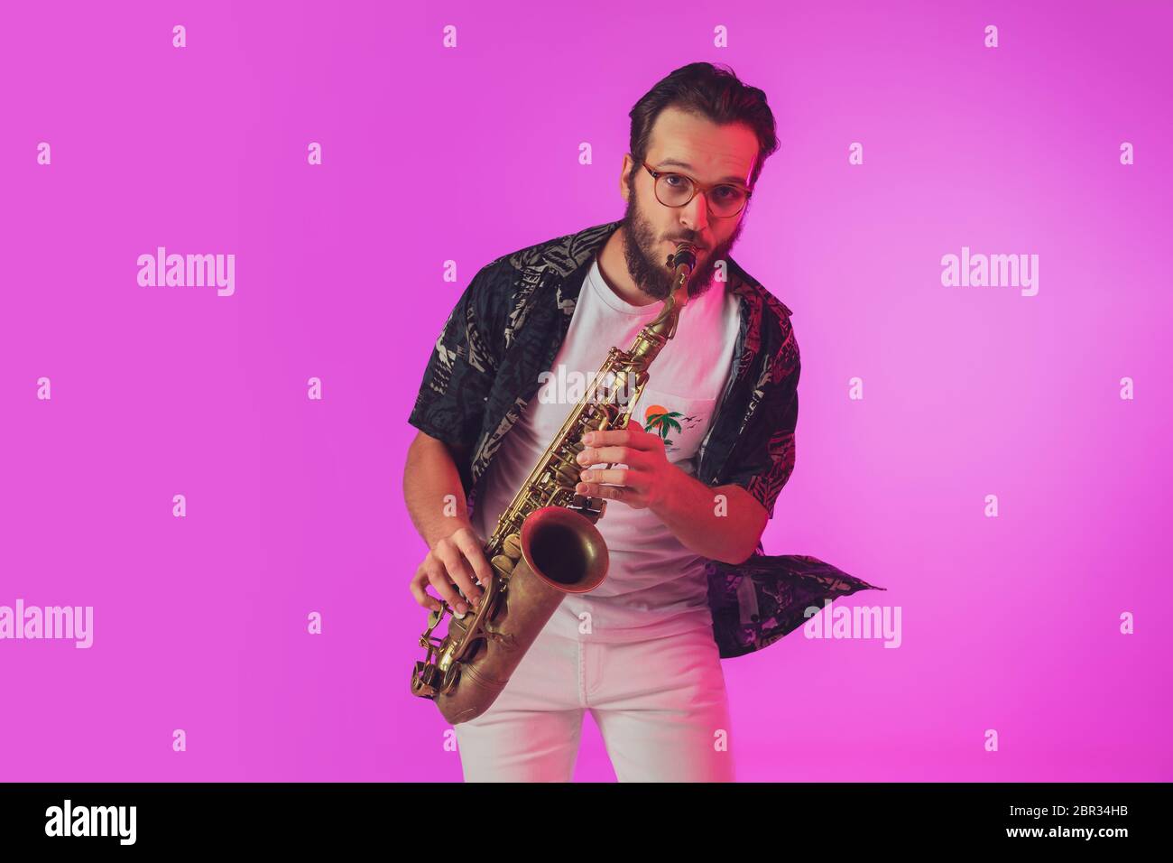 Young caucasian jazz musician playing the saxophone on gradient pink ...