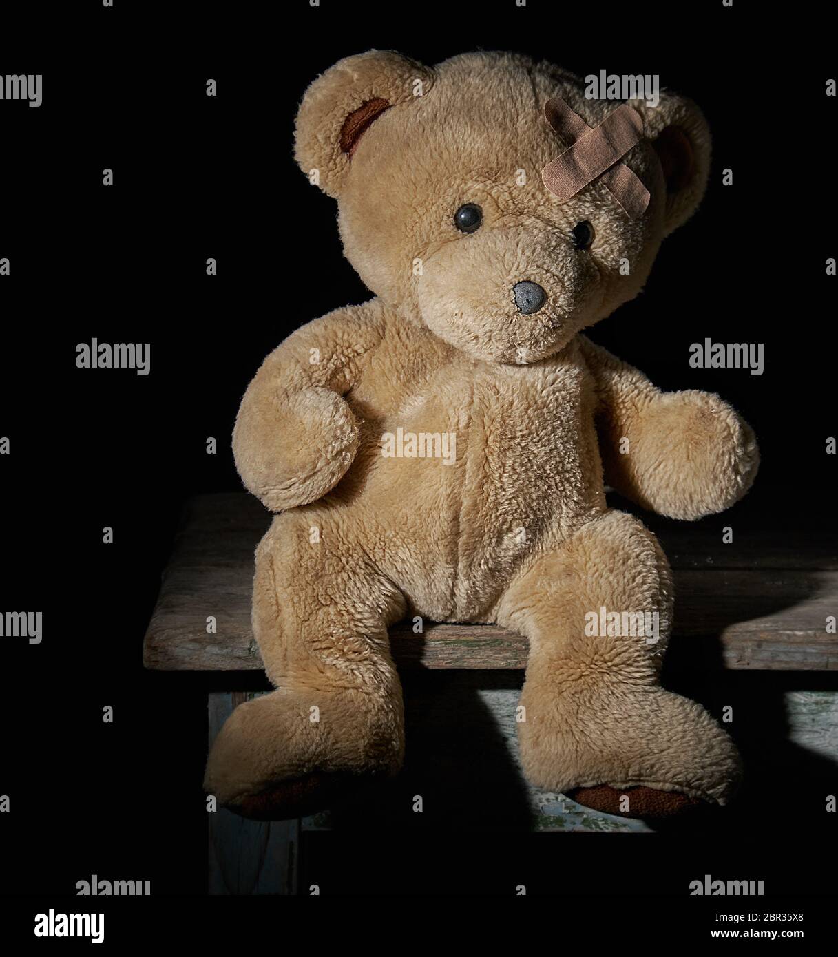 old brown teddy bear is sitting on a wooden surface, plaster is glued ...
