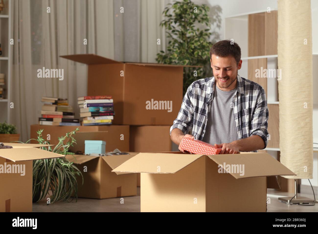 Happy man moving home unboxing belongings on the floor in the night ...