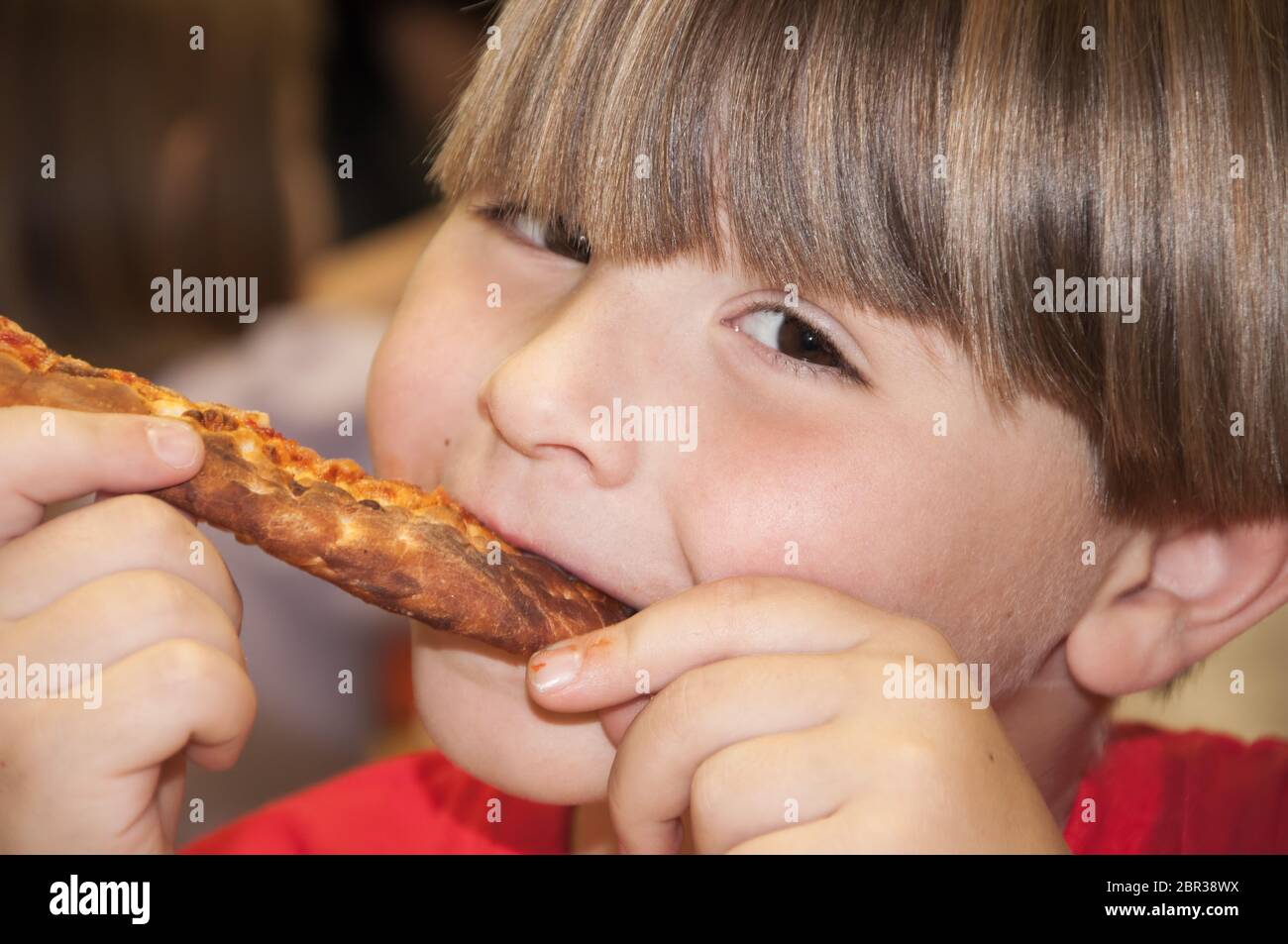 Young boy with a red shirt eating pizza Stock Photo - Alamy
