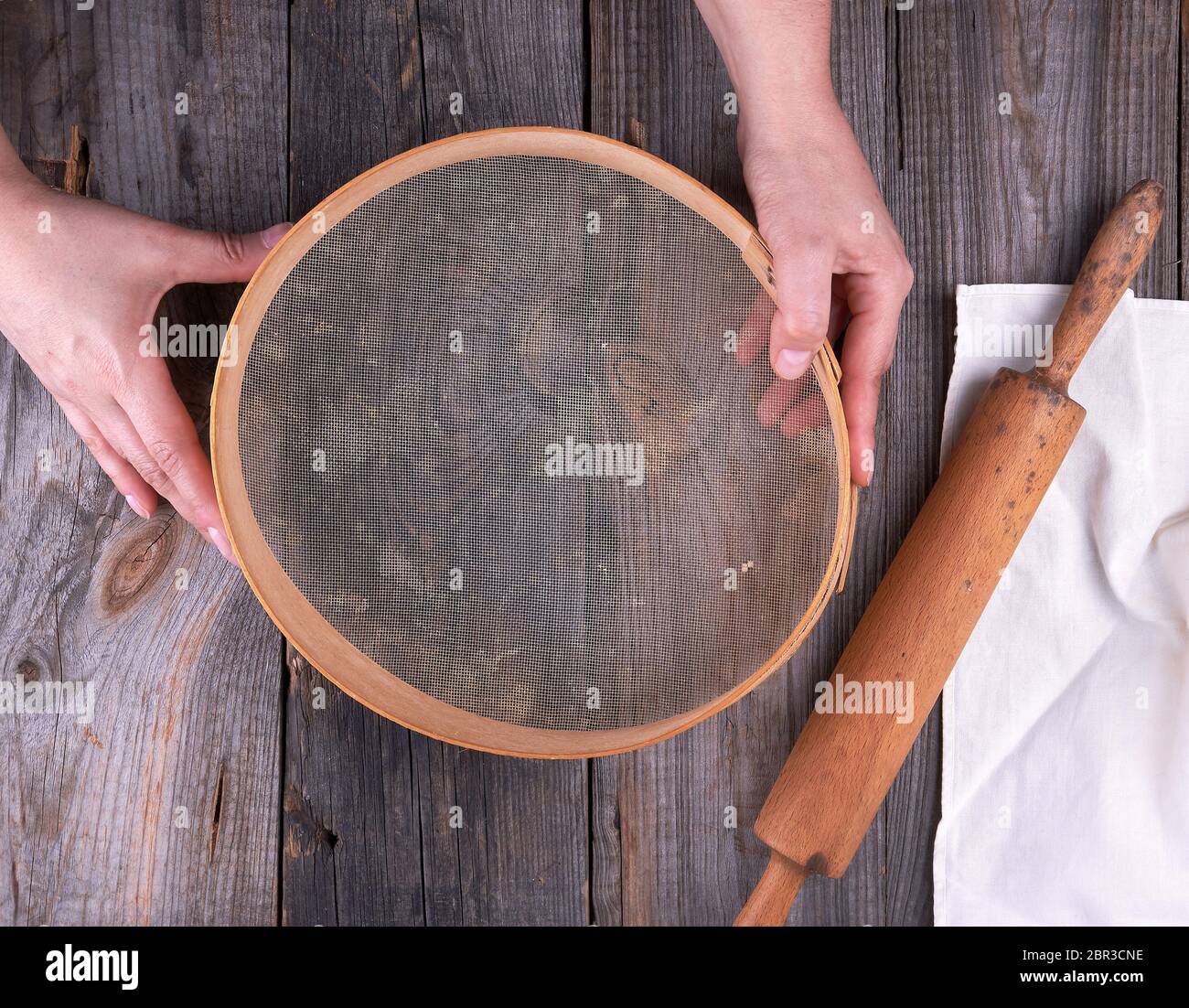 female hands holding a round wooden sieve for flour, next to an old ...