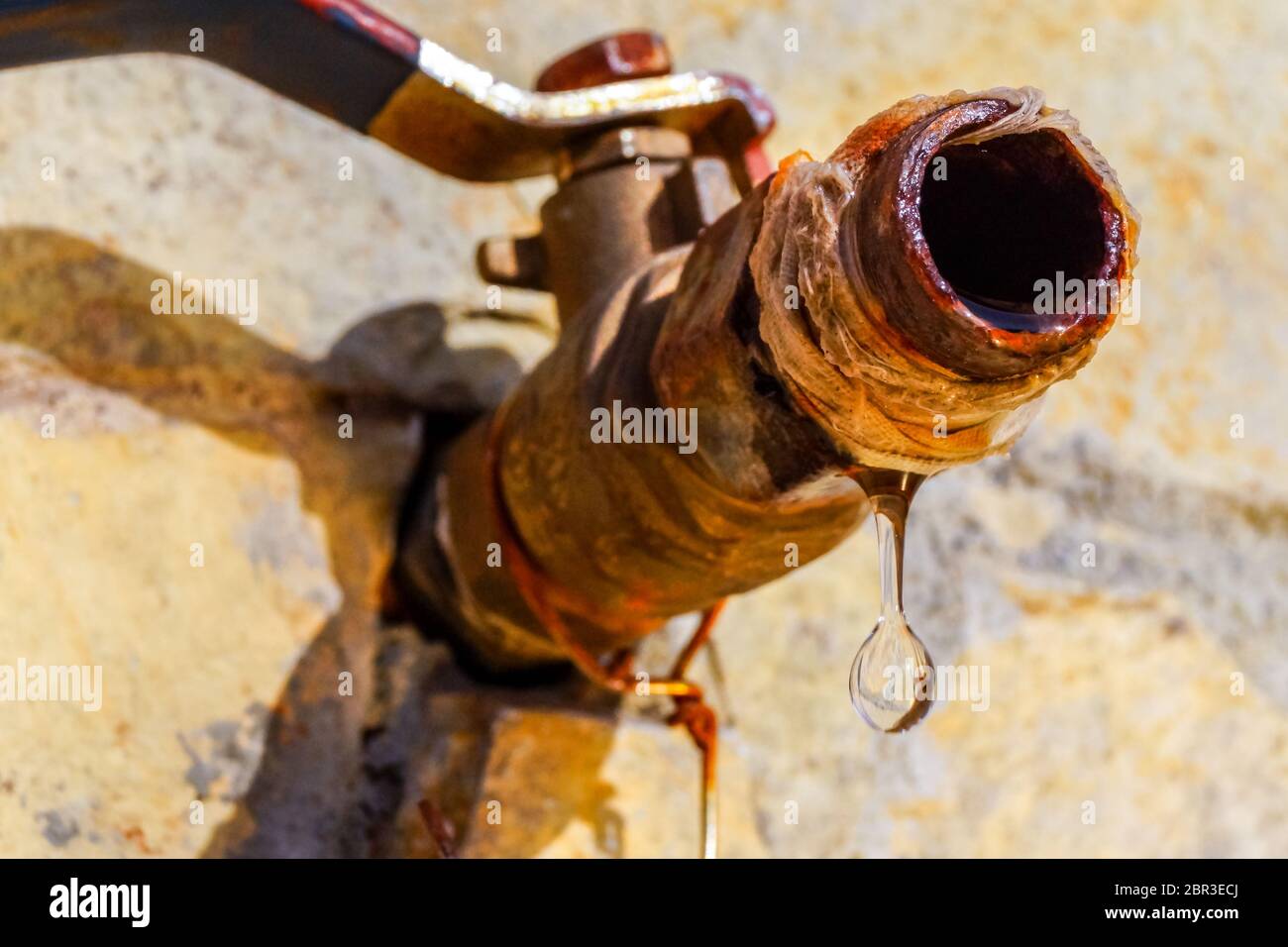 Close up image of a drop of water dripping from a rusty tap. Image can ...