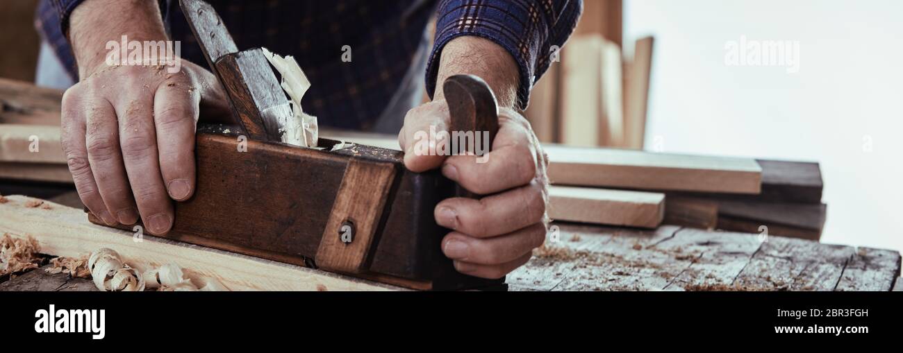 Panorama banner of a carpenter planing wood using an old-fashioned ...