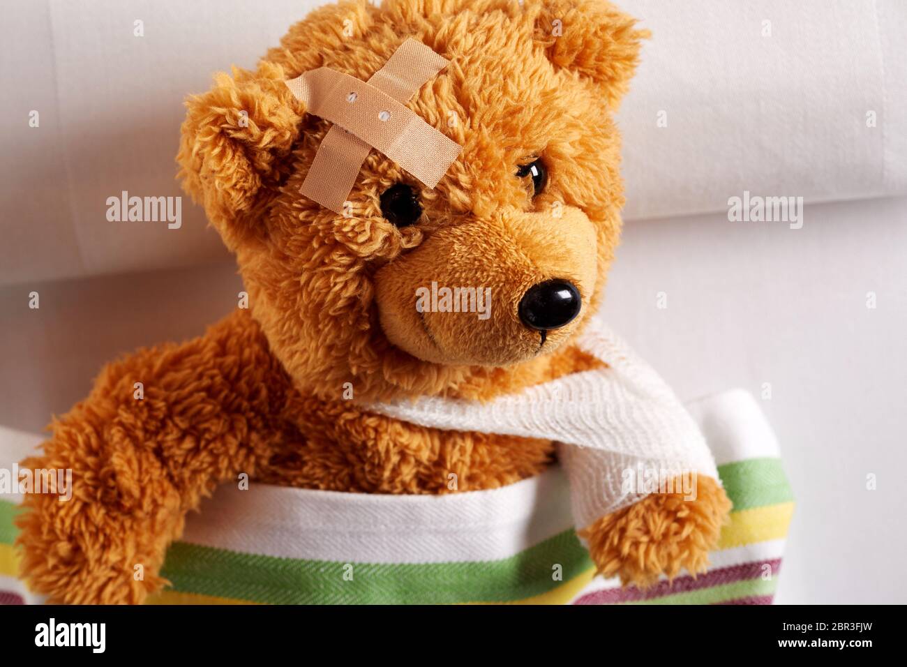 Injured teddy bear with bandaged arm and head lying in bed after an ...