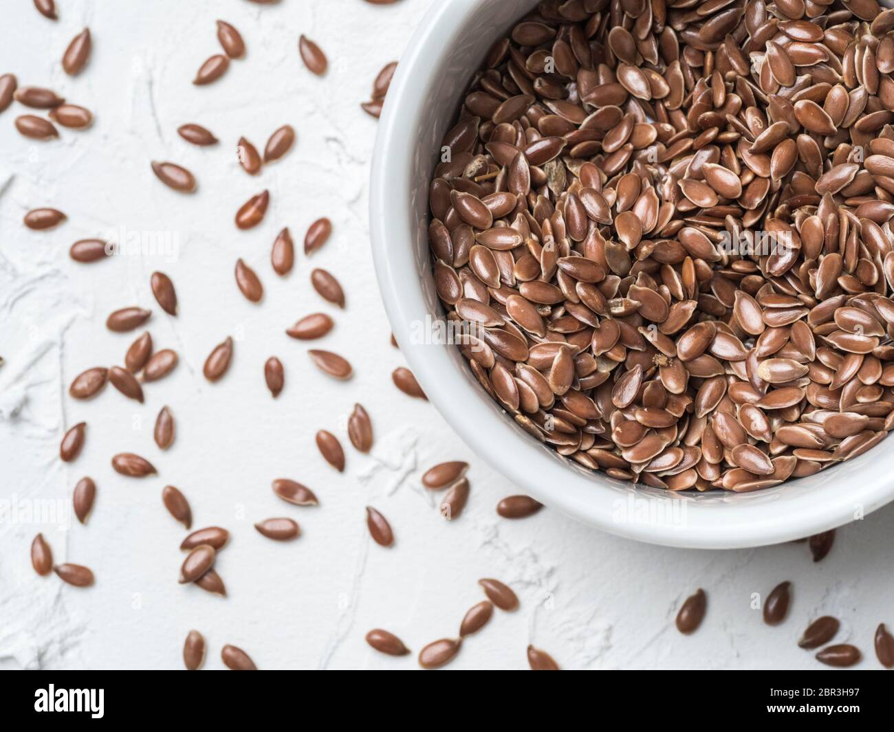 Flax seeds with copy space. Brown flax seed on white concrete textured background. Top view or ...