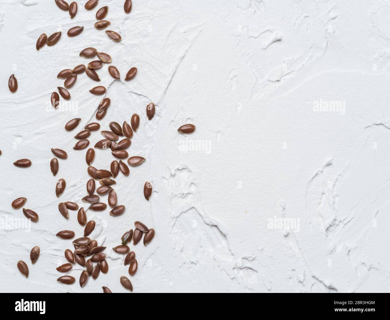Flax seeds with copy space. Brown flax seed on white concrete textured background. Top view or ...