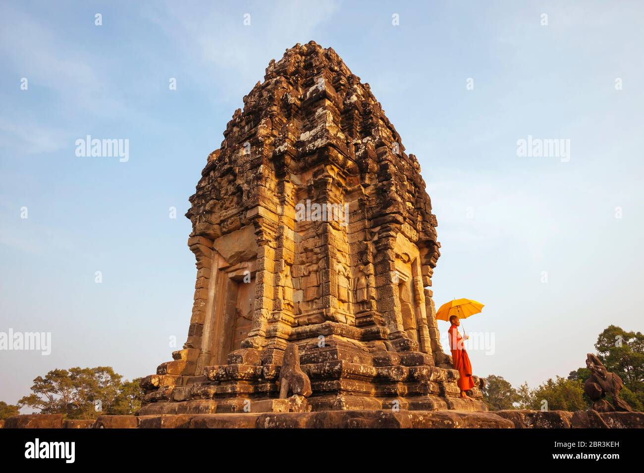 A Monk stands with shade umbrella at the side of a temple at Roluos ...