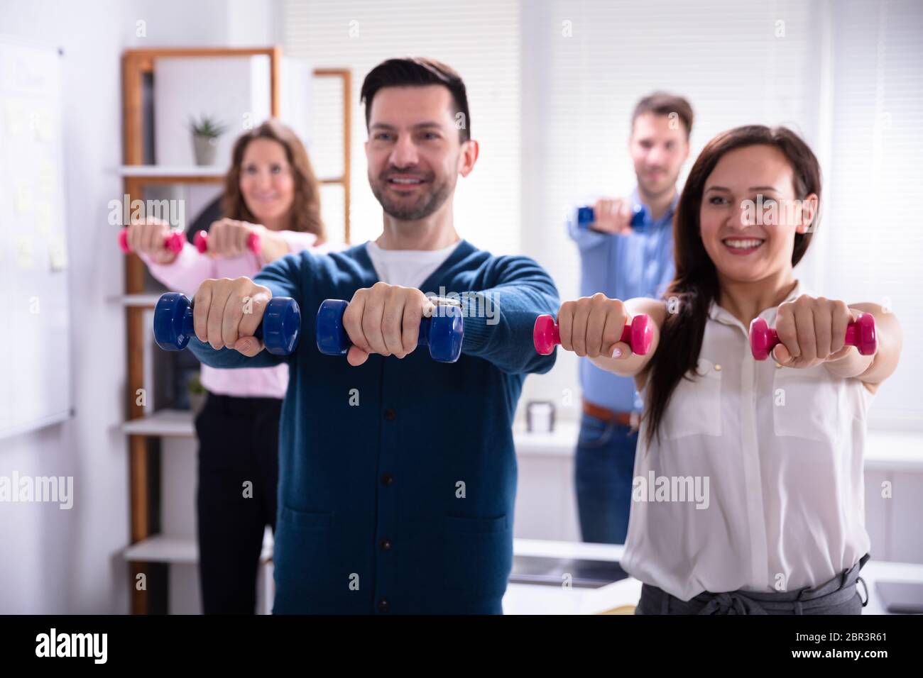 Young Businesspeople Exercising With Dumbbells In Office Stock Photo ...