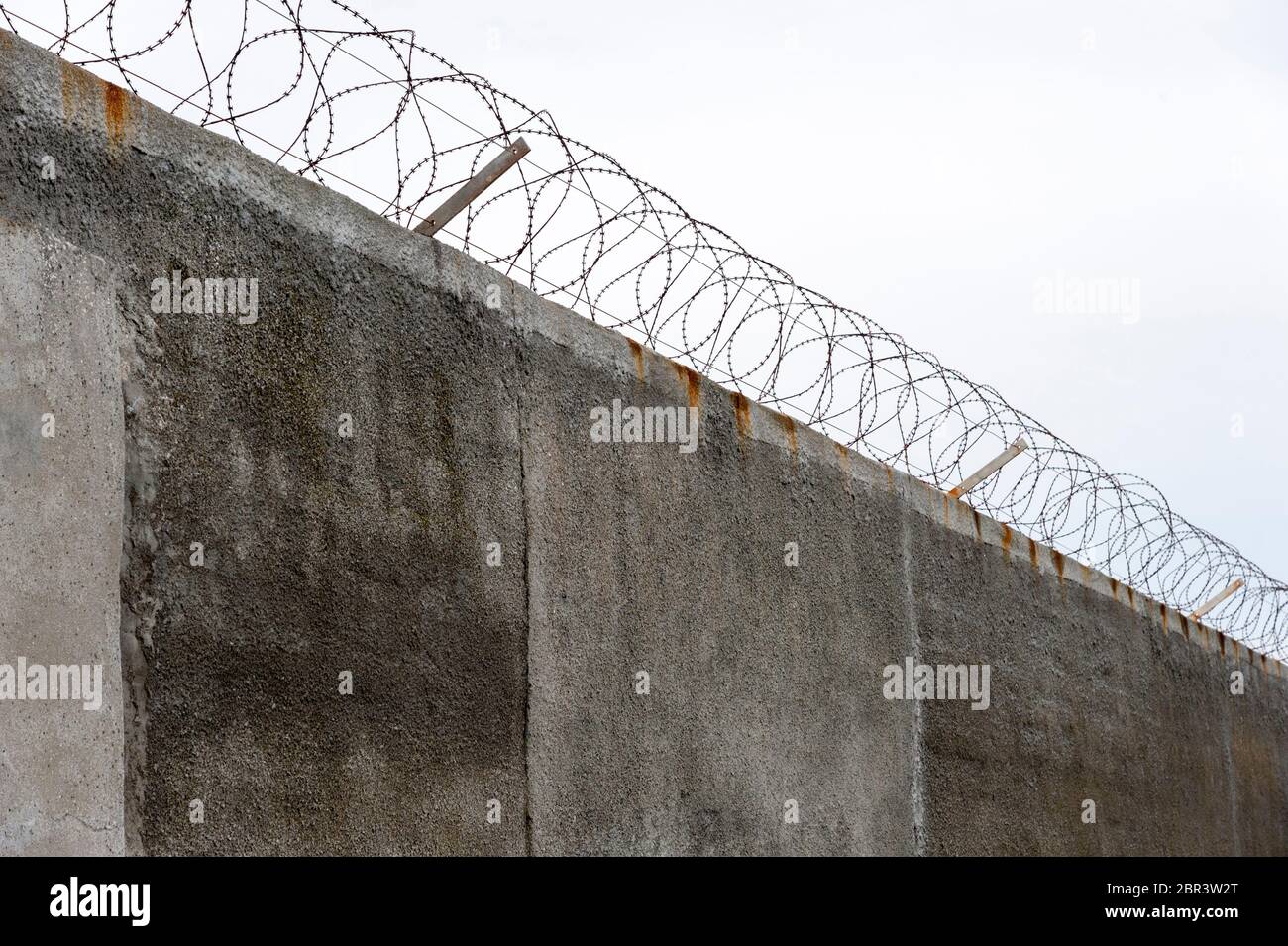 Concrete grey prison wall with barb wire Stock Photo - Alamy