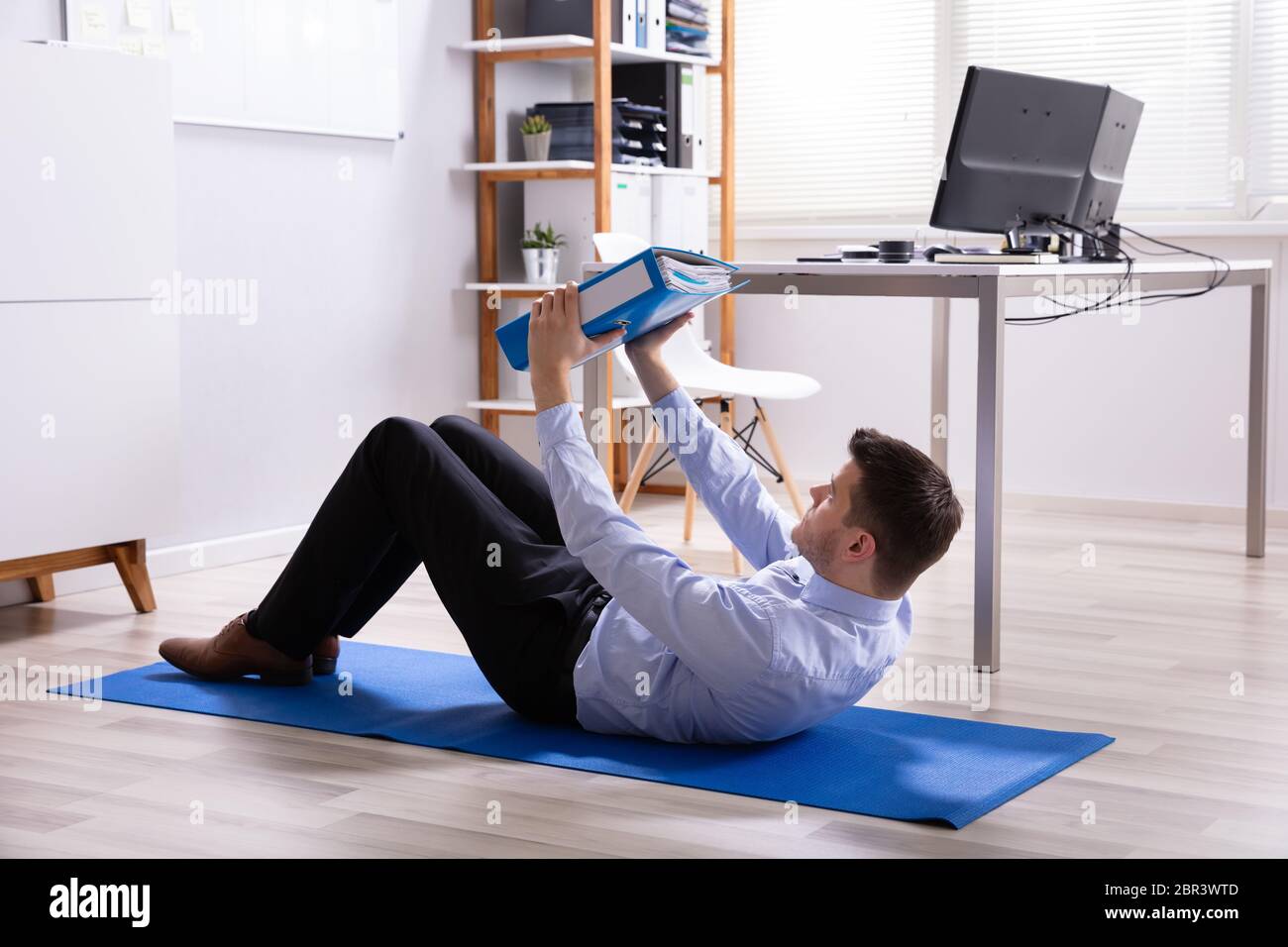 Businessman Doing Situps In Office Holding Folder File In Hand Stock ...