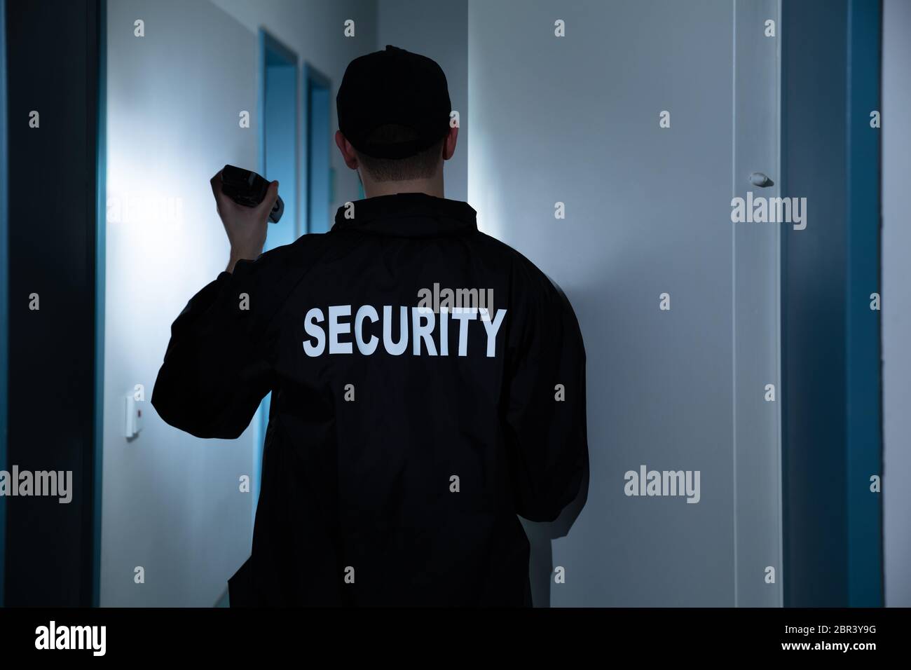 Rear View Of Male Security Guard With Flashlight Standing In Corridor ...