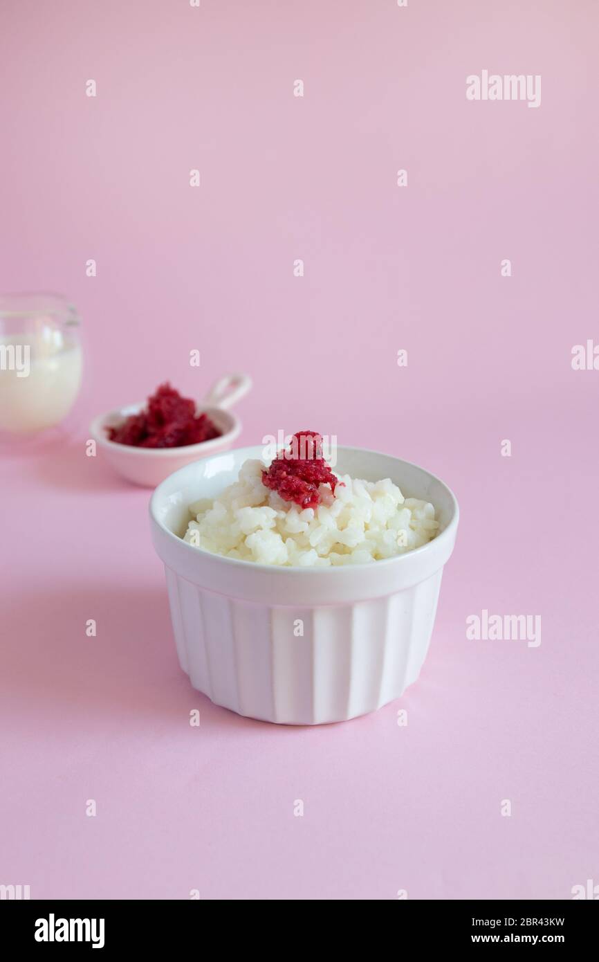 Milk rice porridge with frozen berries on a pink background, vertical ...