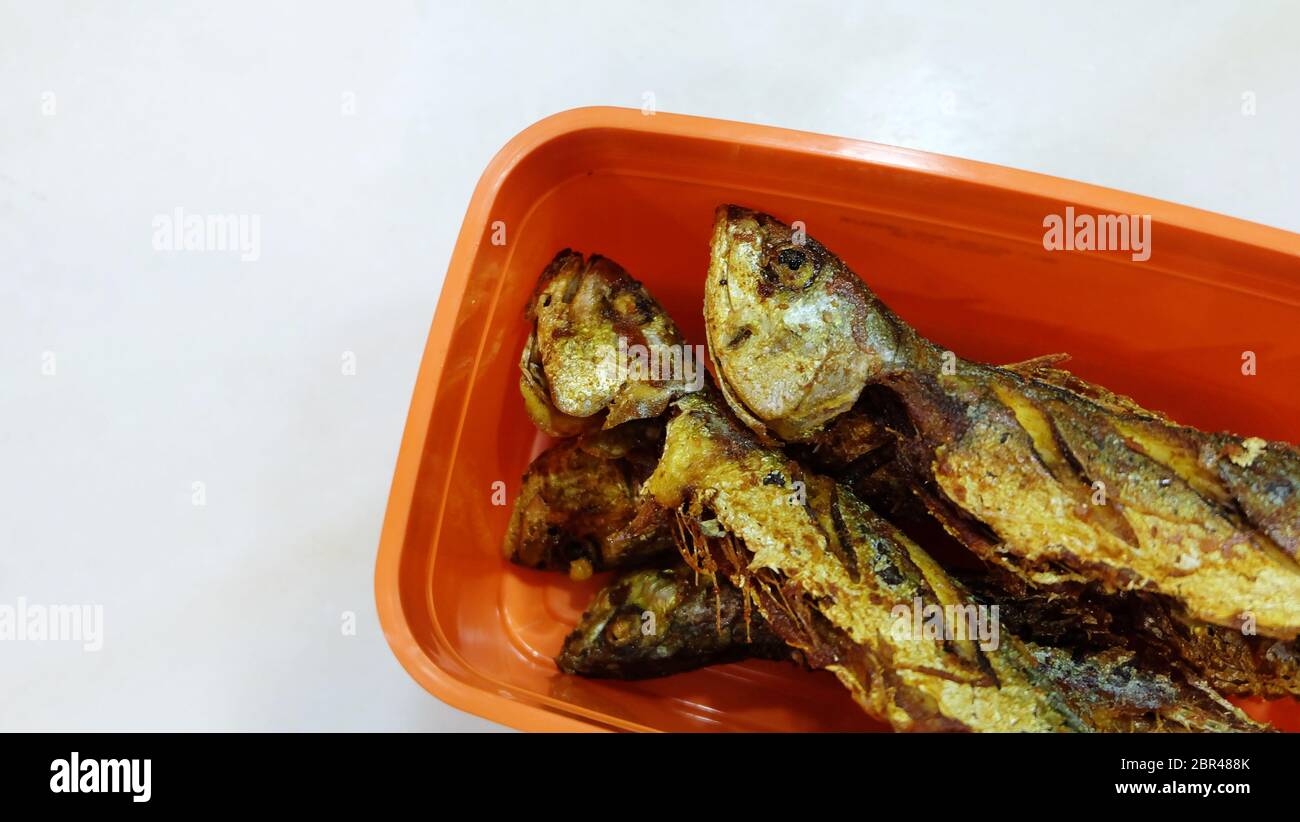 Fried shrimp scad fishes in a red plastic container, on a marble ...