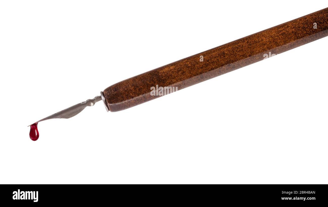 side view of red ink drop dripping from nib of brown dip pen close up ...