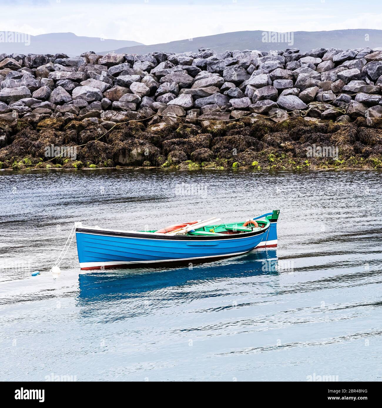 Reflection of a blue rowing boat in front of a wall of boulders Stock ...
