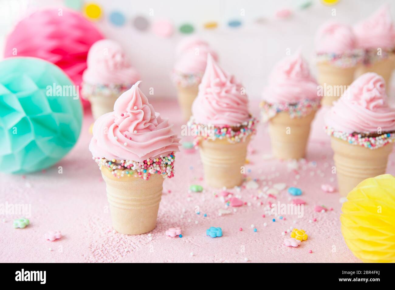 Pink soft serve ice cream with colorful sprinkles in little waffle cups ...