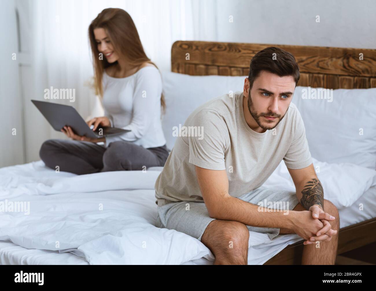 Jealousy concept. Girl typing on laptop, sad guy sitting on bed Stock ...