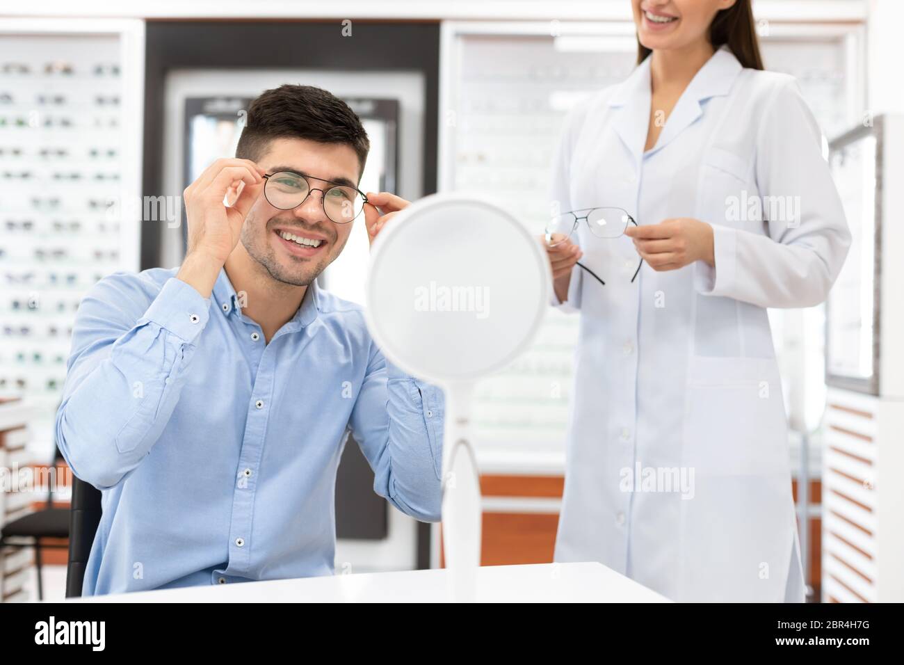 Optometrist helping young guy to choose correction glasses Stock Photo ...