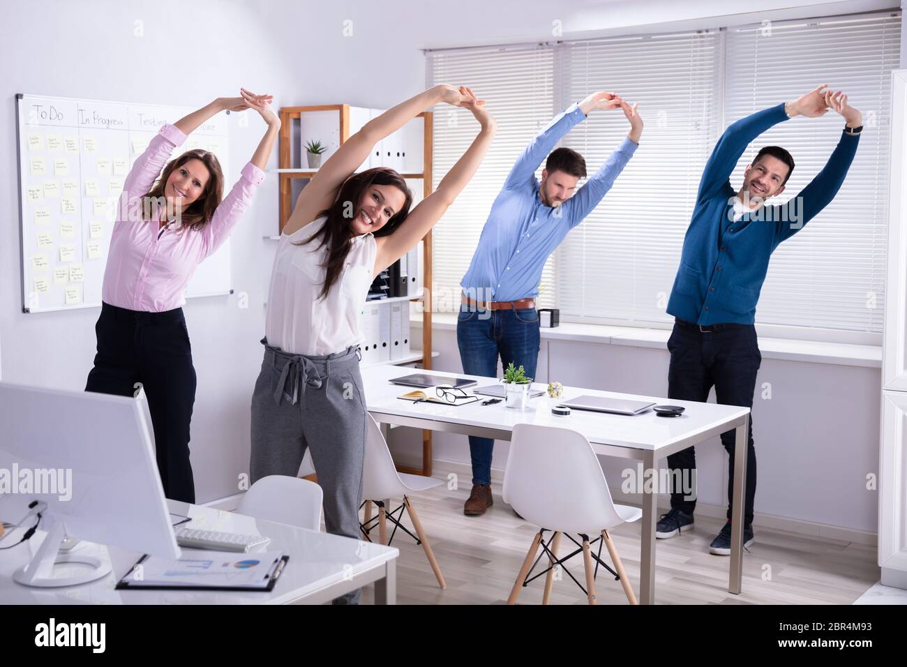 Happy Businesspeople Doing Stretching Exercise Behind Desk At Workplace ...