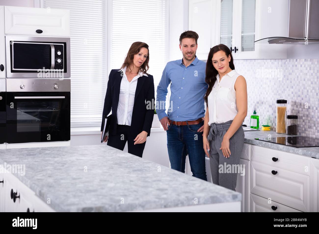 Young Woman Checking Kitchen Cabinet During Meeting With Real Estate ...