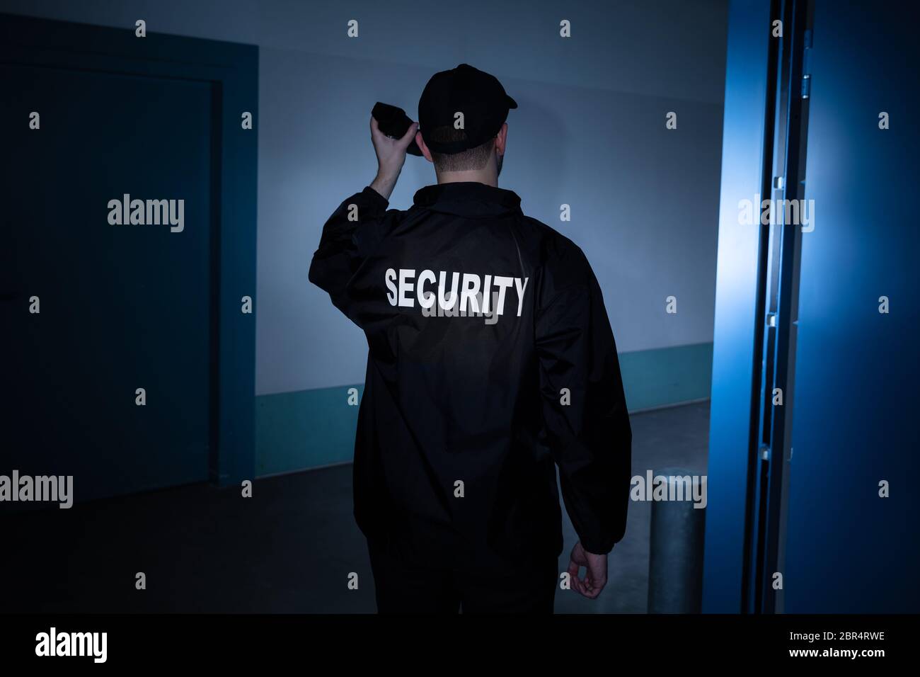 Rear View Of A Male Security Guard With Flashlight Standing In Corridor ...