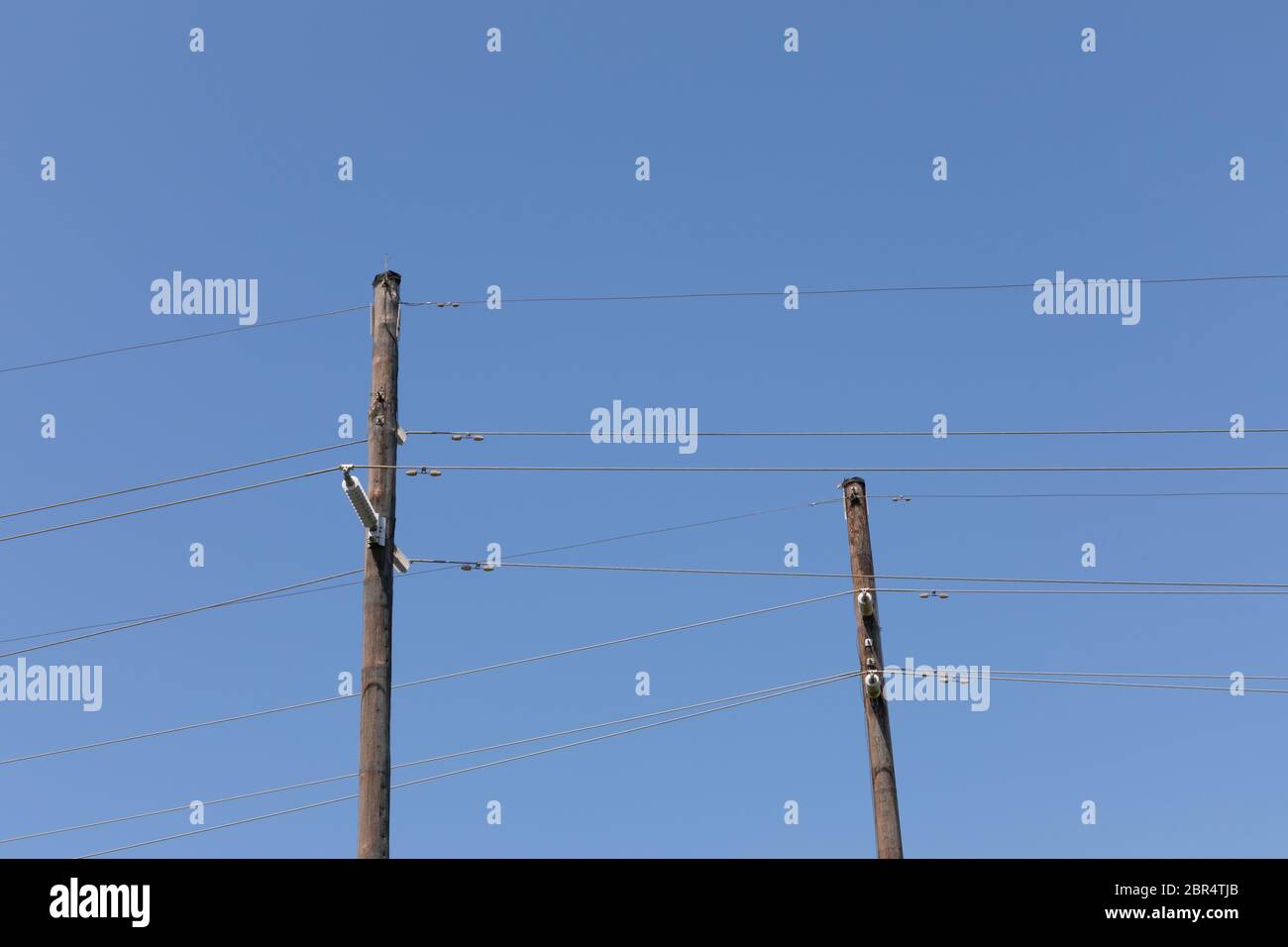 Two tall wooden power poles with lines, strain insulators, against a ...