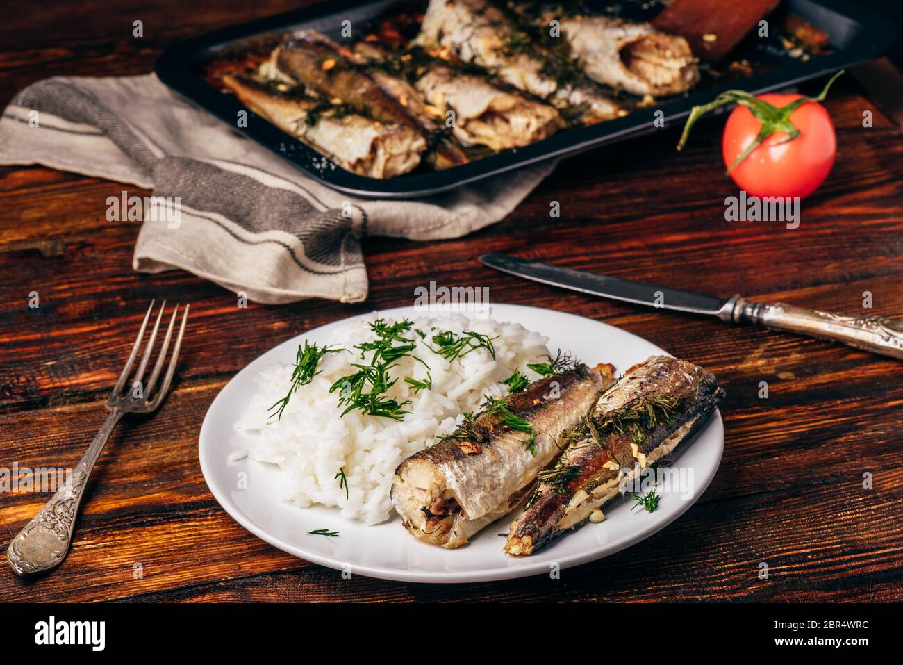 Baked hake carcasses with rice on white plate Stock Photo - Alamy