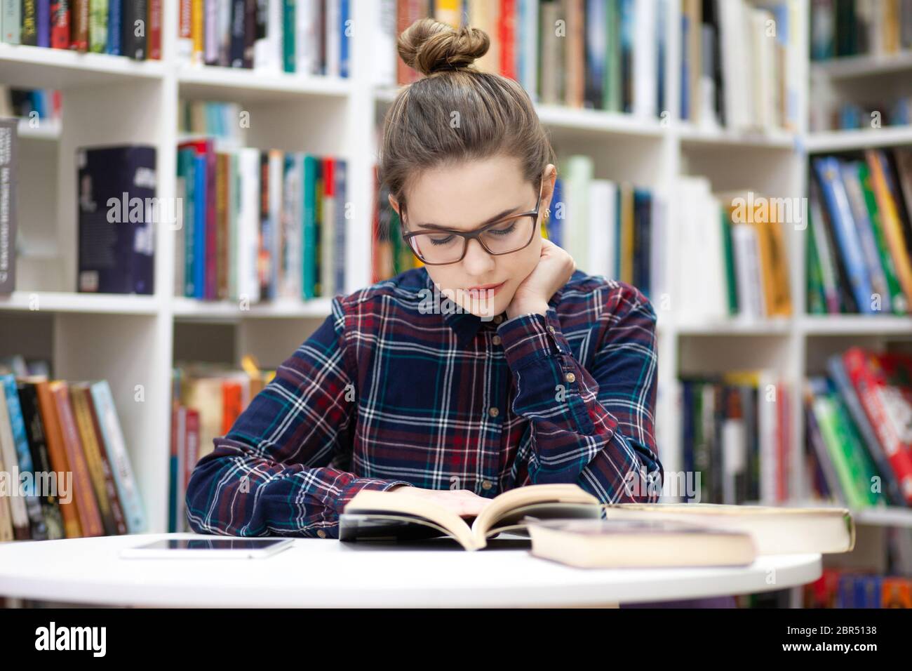 Girl sitting in the library. Young student in glasses in a checkered ...