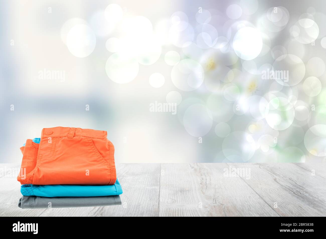 Stack of colorful short pants for kids on bright wooden table in front ...