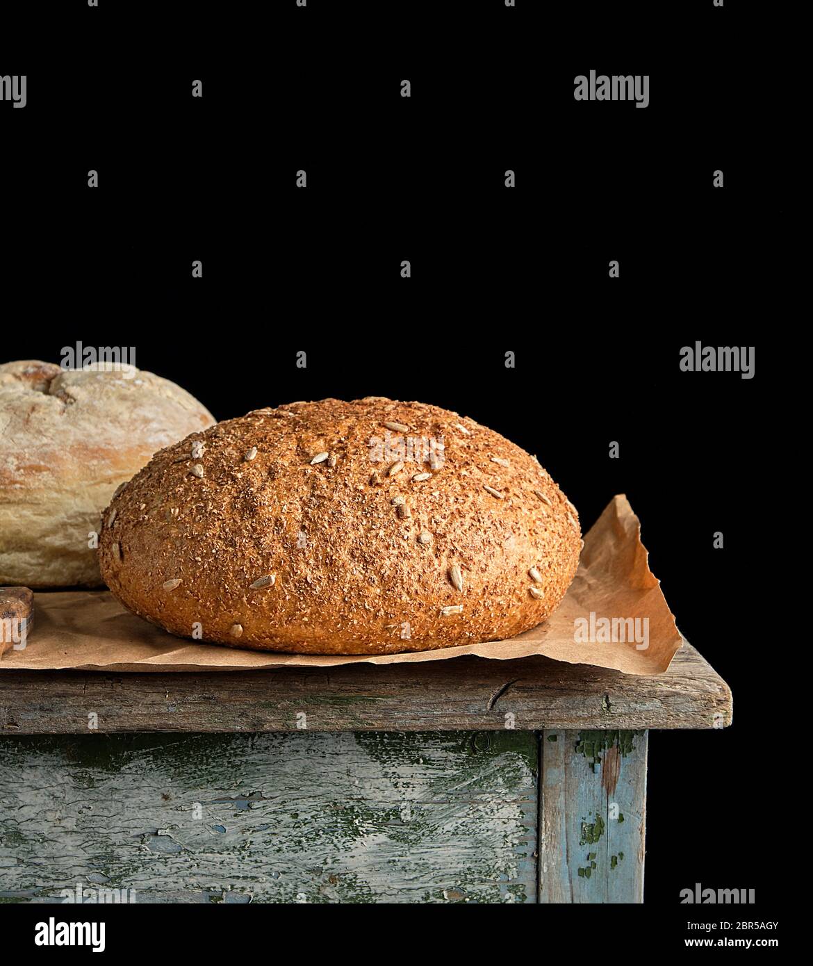 baked round rye bread with sunflower seeds lies on a brown paper, black ...