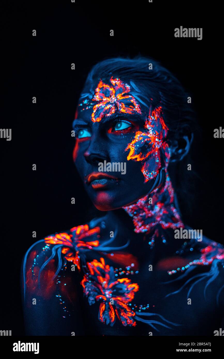 Conceptual face art with shining flowers painted in fluorescent colors ...